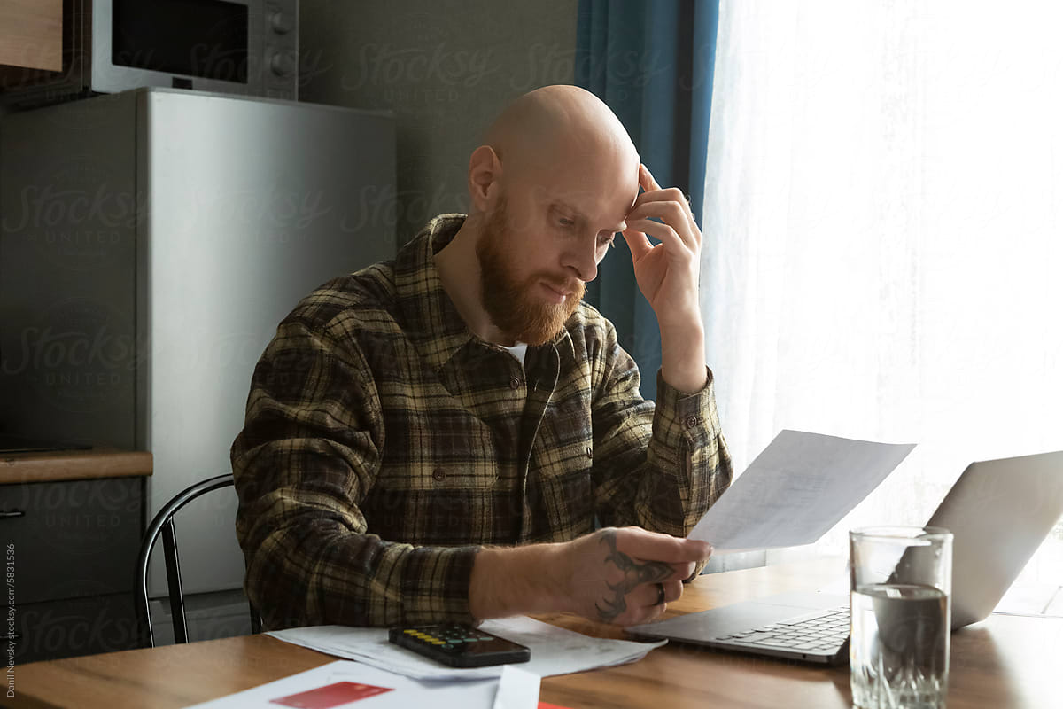 "Focused Man Reading Paper At Table With Laptop And Water Glass" by ...