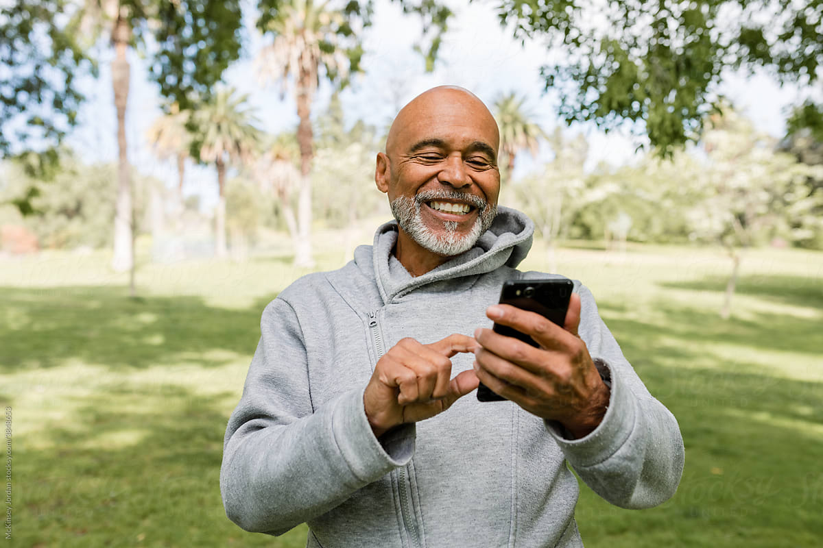  Older Man Laughs While Texting On His Phone At The Park By Stocksy