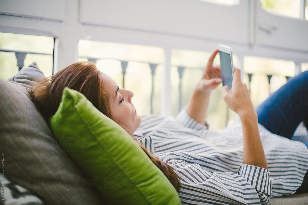 "Woman Chatting On Her Phone Lying On Sofa At Home." by Stocksy ...