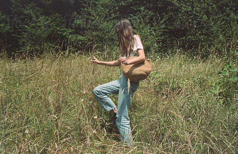 young woman frolicking in a field in jeans with a bag - Stock Image ...