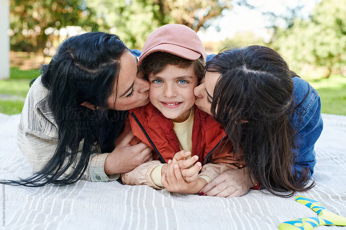 "Two Moms Kissing Their Son On A Blanket Outside" by Stocksy ...