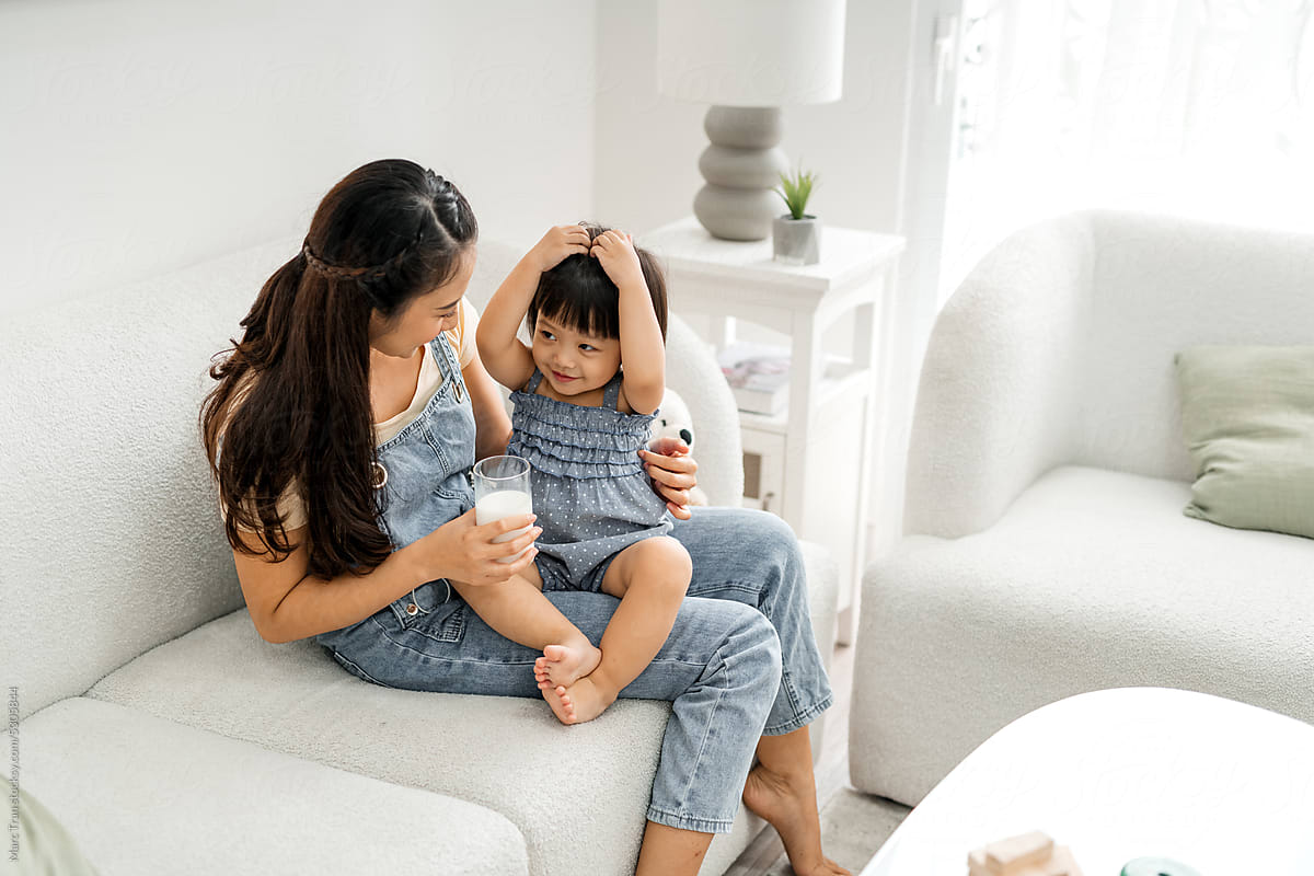 "Young Nanny Sitting On Couch Serving Milk With Little Girl" by Stocksy ...