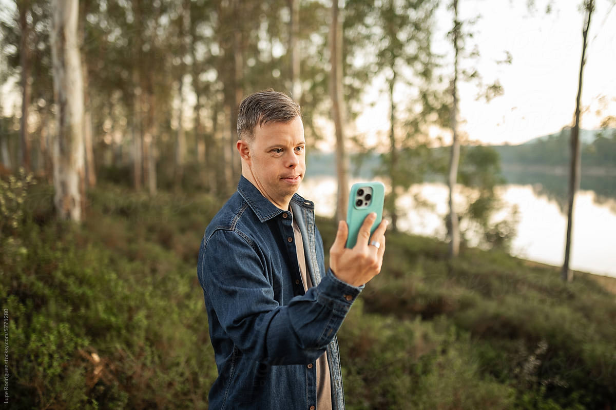 man with down syndrome using his mobile phone in a forest in nature ...