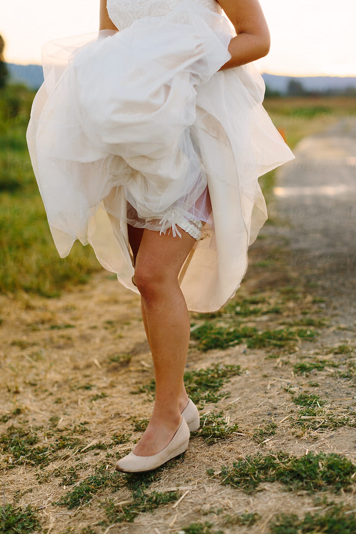 Bride Holding Up Dress And Walking In Field By Stocksy Contributor bride-holding-up-dress-and-walking-in-field-by-stocksy-contributor