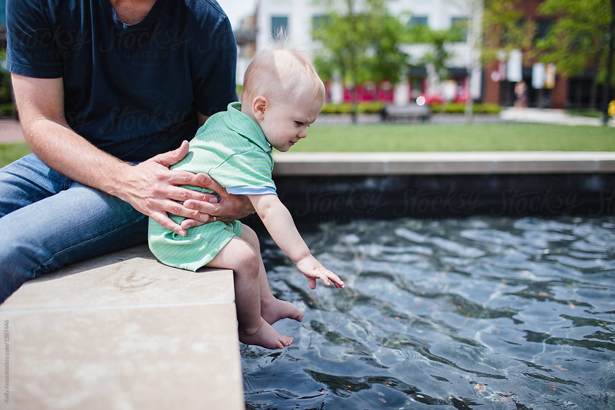 "Father Holding Baby Who Is Reaching To Touch The Water" by Stocksy ...