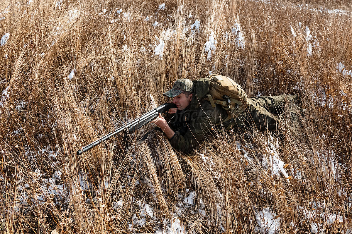 Hunter lying on grass and snow and shooting - Stock Image - Everypixel