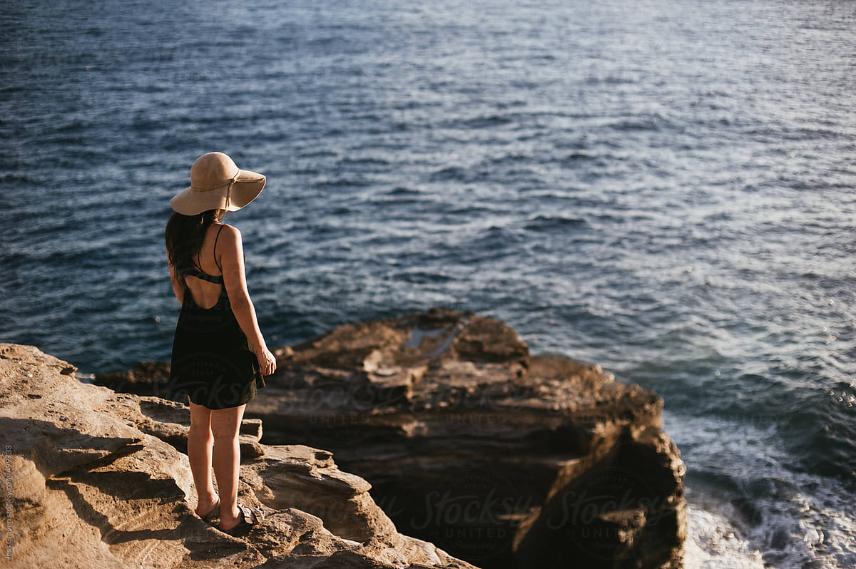 "Girl Standing On Edge Of Cliff Overlooking Sunset On Pacific Ocean In ...