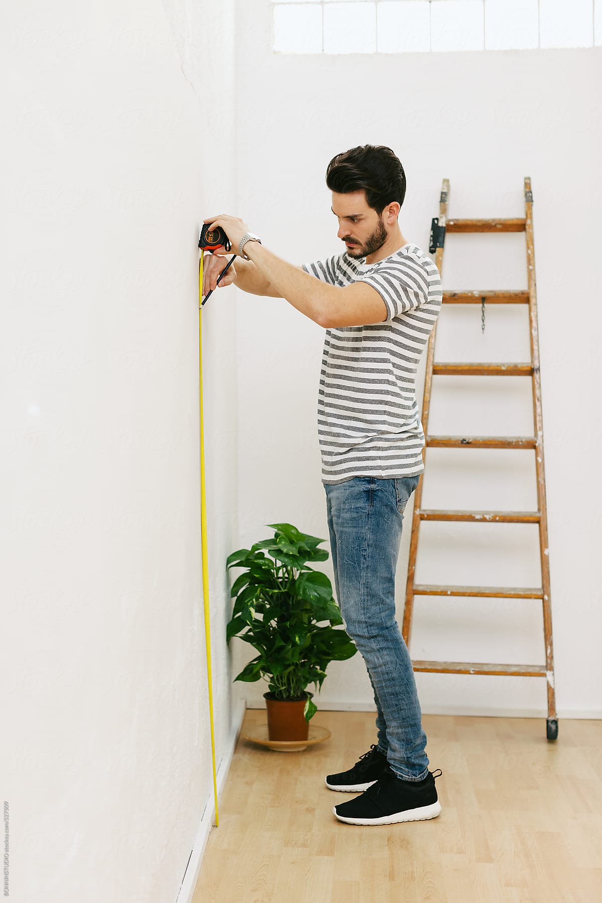 "Young Man Measuring The Wall With Tape Measure ." by Stocksy ...