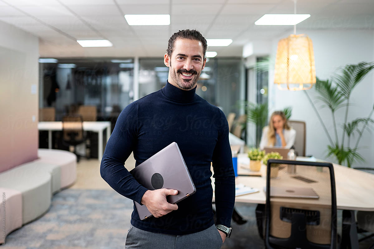 "Portrait Of Handsome Man In An Office Holding A Laptop." by Stocksy ...