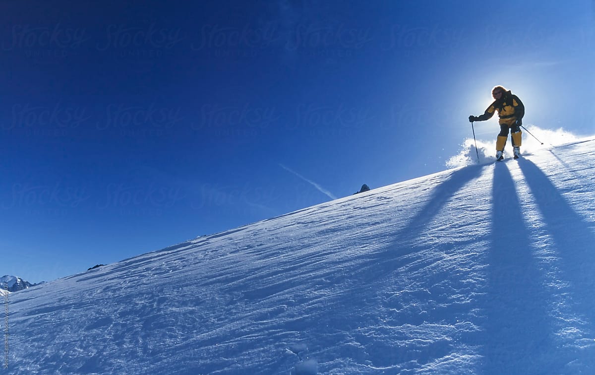 Man skiing powder snow in winter mountains backlit by sun and blue sky ...