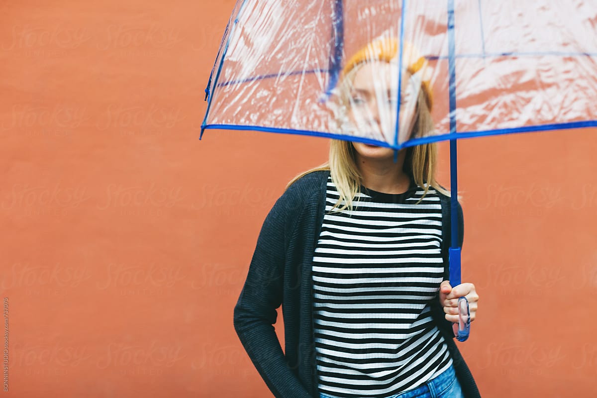 "Woman Covering Her Face With An Umbrella In Front Of An Orange Wall ...