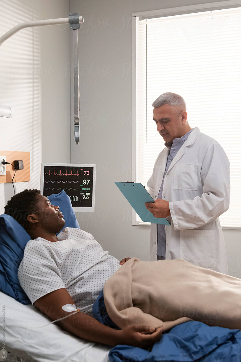 "Doctor Visiting Patient In Hospital Bed And Reading Notes" by Stocksy ...