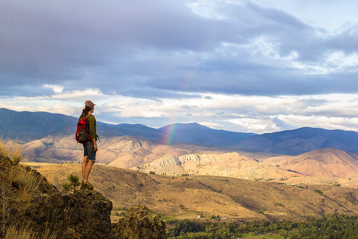"Woman Stands On A Cliff Edge Looking Out At The Mountainous Scenery Of ...