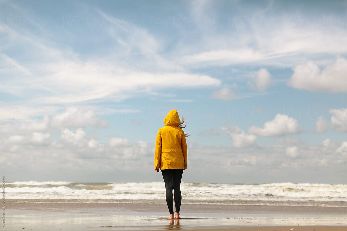 "Person Looks Over The Ocean On A Windy Beach Wearing A Yellow Raincoat ...