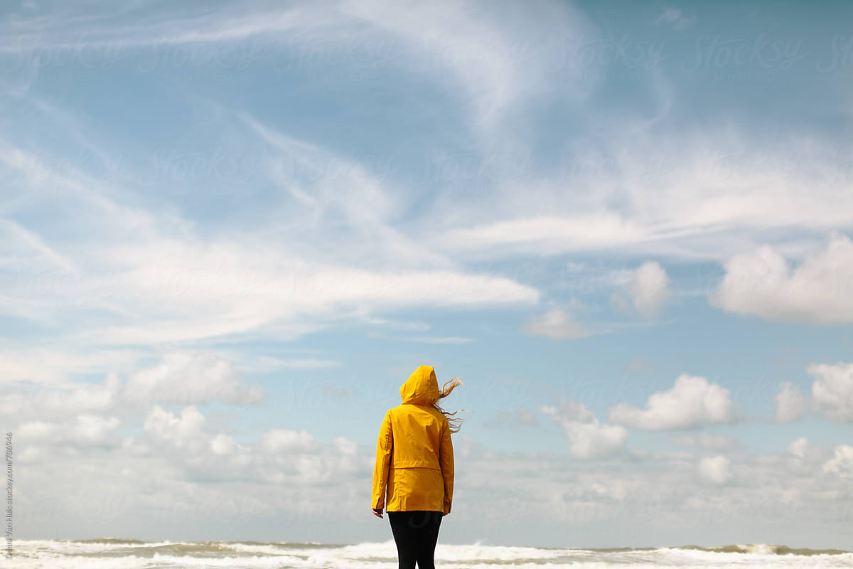 "Person Looks Over The Ocean On A Windy Beach Wearing A Yellow Raincoat ...