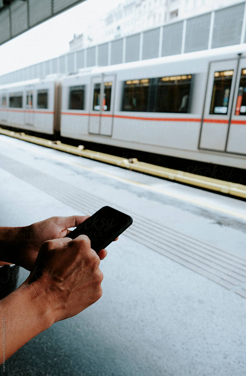 is using his smartphone on the train platform - Stock Image - Everypixel