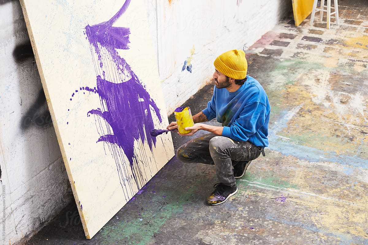 "Mid Adult Artist Painting On Canvas While Crouching In Studio" by ...