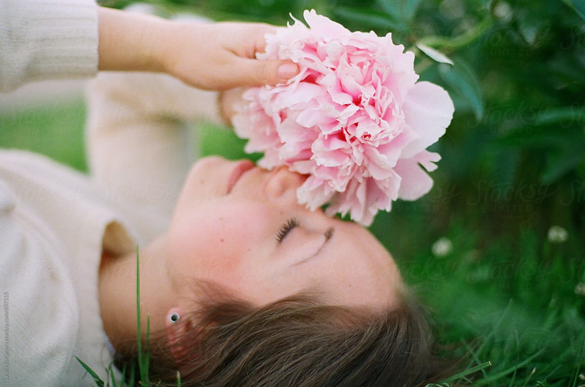 "Young Woman Lying On Grass And Smelling Pink Peony" by Stocksy ...