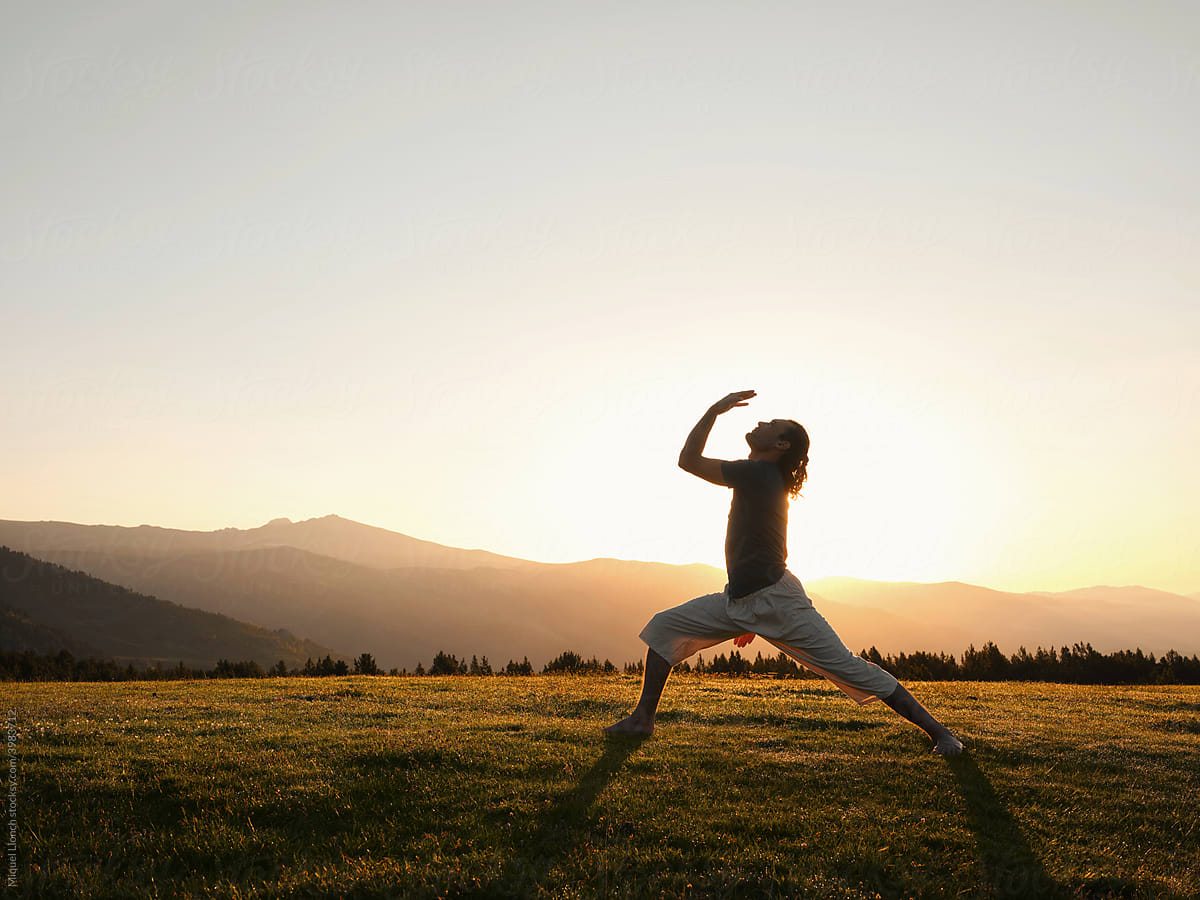 Man in Warrior pose with Eagle hands on meadow in early morning - Stock ...