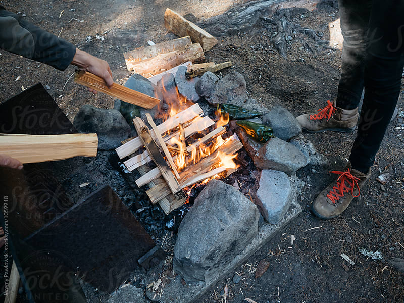 Man putting log on campfire in the woods with woman watching - Stock ...