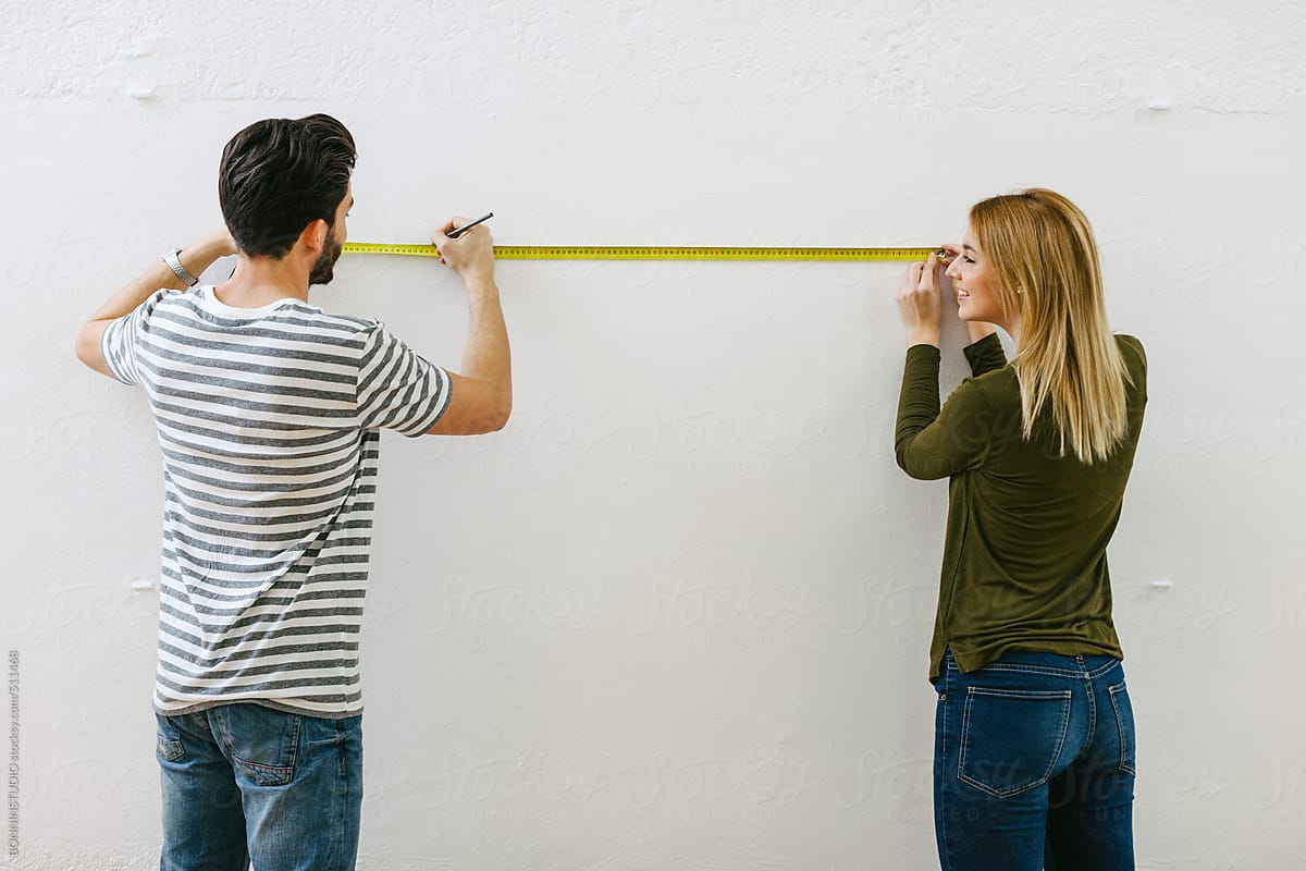 "Young Couple Measuring The Wall To Hanging A Picture." by Stocksy ...
