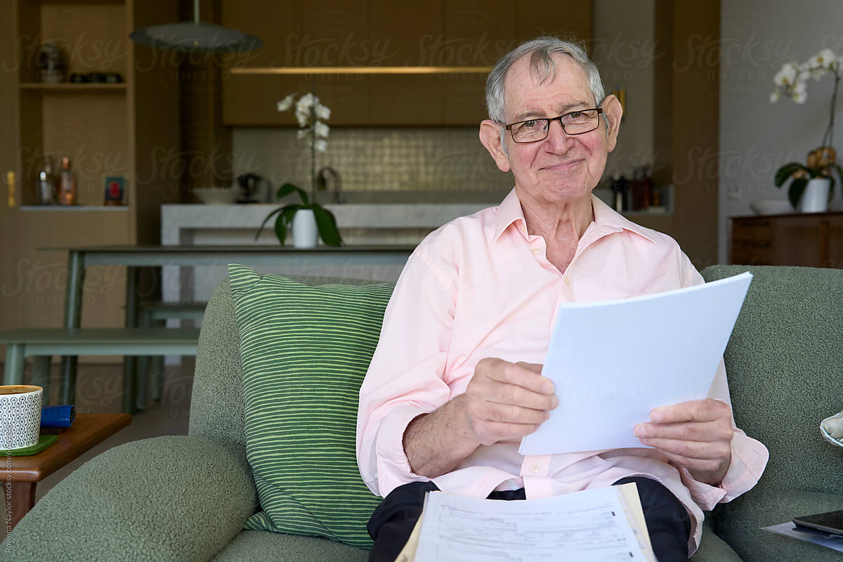 "Senior Man Smiles While Reviewing Documents In A Modern Living Room ...