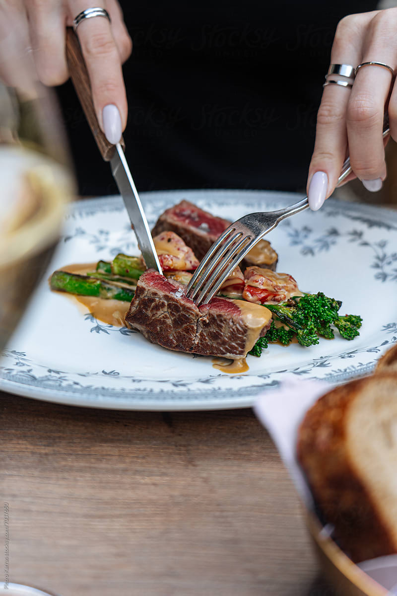 "Person Cutting Medium-rare Steak With Vegetables And Sauce On Plate ...