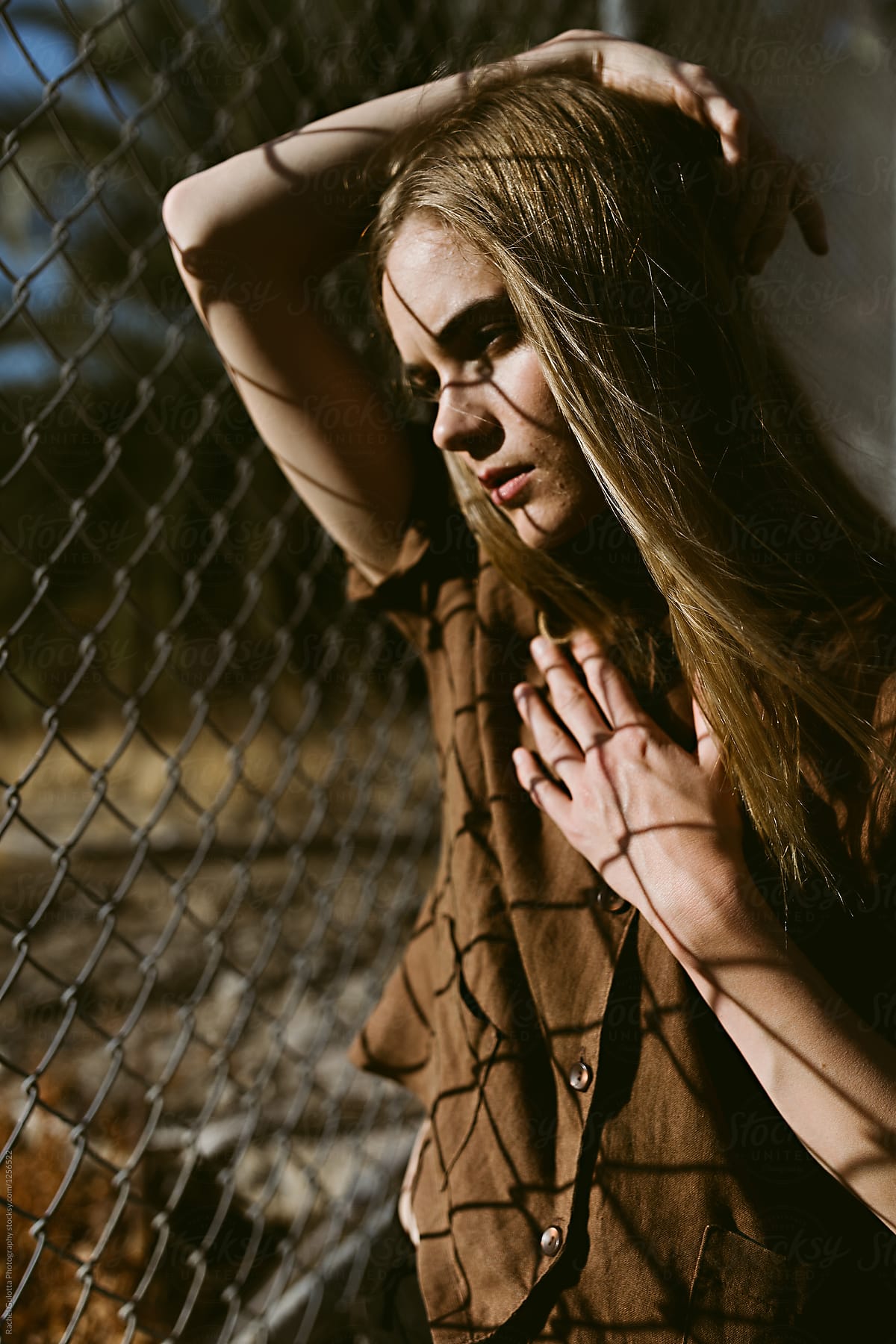 "Woman Standing In Front Of A Fence With Shadows And Harsh Light On Her ...