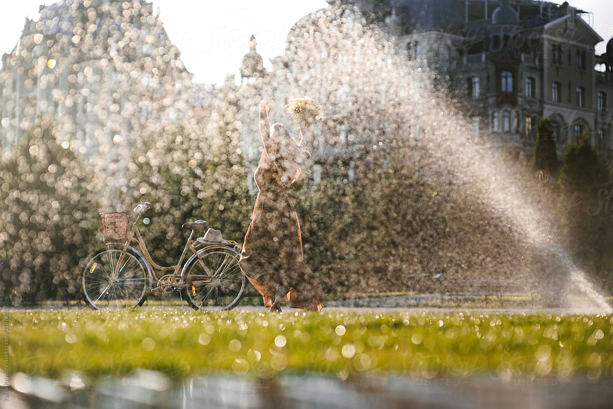 "Young Woman Dancing Under The Flower Watering Spray In The Park" by ...