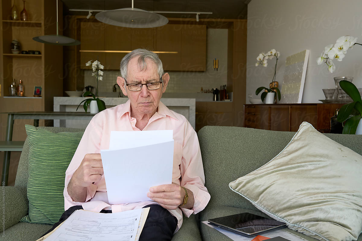 "Elderly Man Reviewing Documents On A Sofa In A Modern Room" by Stocksy ...