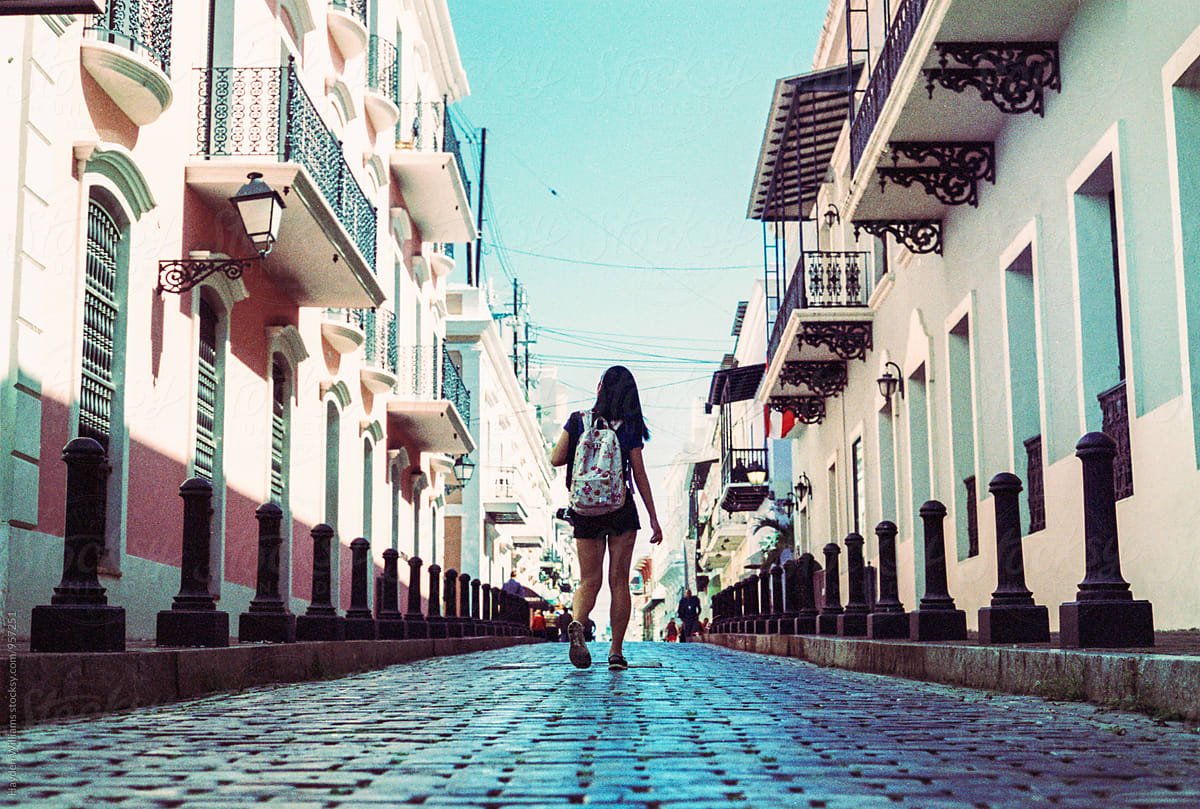 "Girl Walking Down Cobblestone Street Surrounded By Colorful Buildings ...