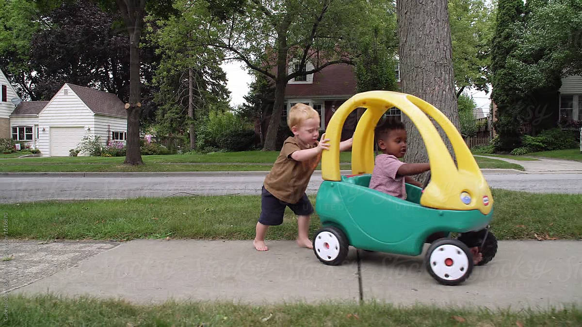 "Caucasian Boy Pushing A Black Boy In A Toy Car On The Sidewalk" by ...