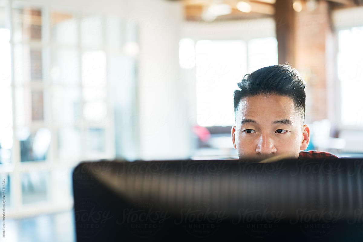 "Casual Young Asian Man Sits At Computer Looking At Monitor In A" by ...