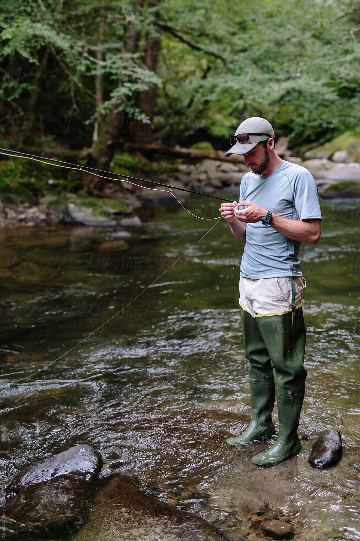 Man fly-fishing in clear river tying fly to line - Stock Image - Everypixel