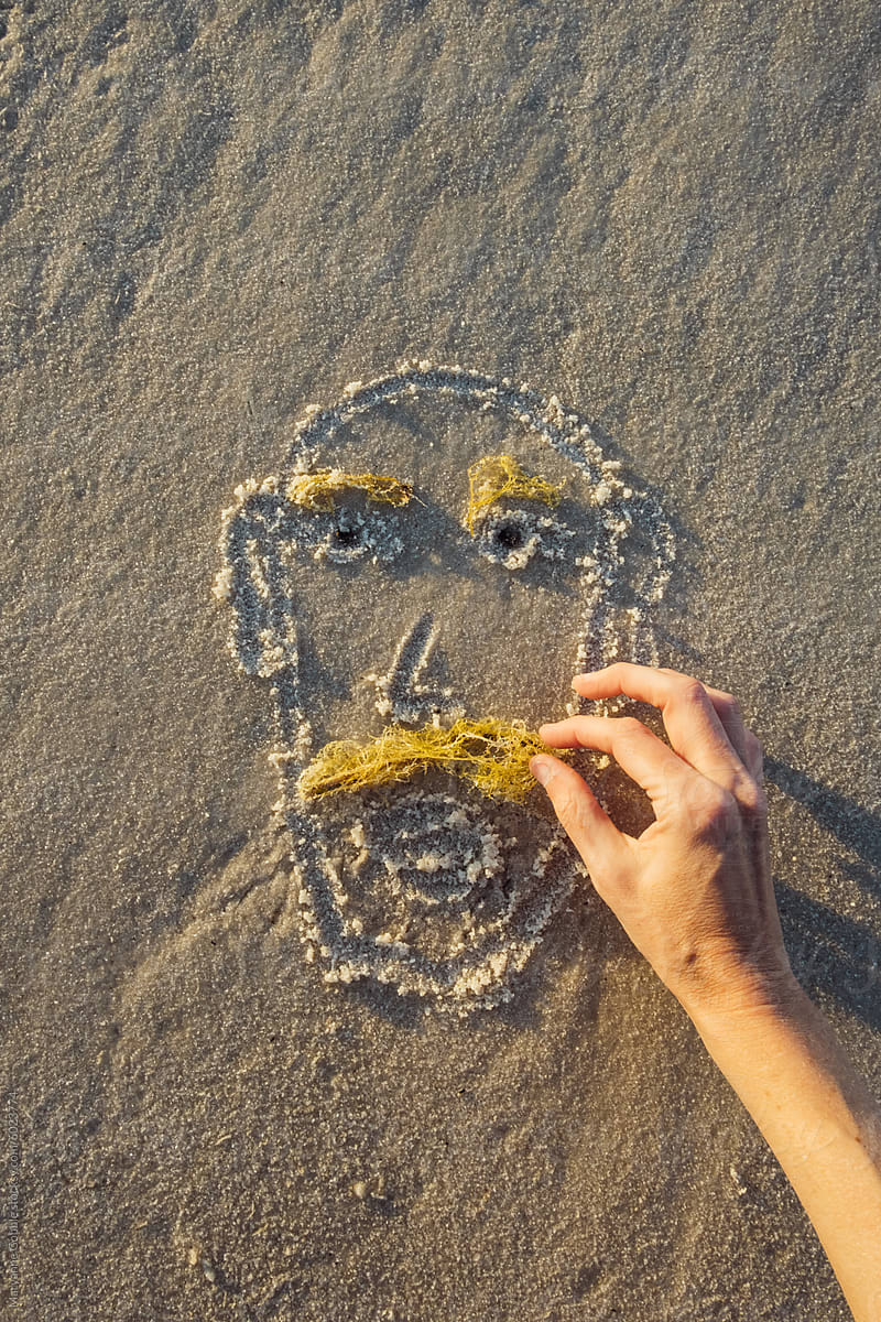 "Face With Mustache And Seaweed Eyebrows Drawn In Beach Sand" by ...