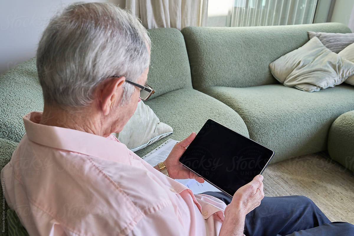 "Senior Man Using An IPad While Sitting On A Green Couch At Home" by ...
