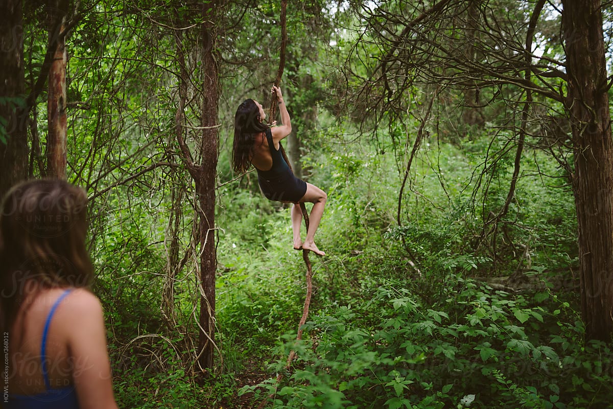 "A Young Girl Climbs Up A Vine In A Forrest Full Of Lush Green Plants ...