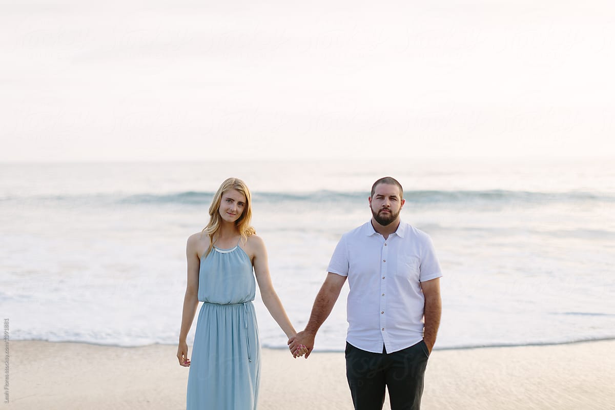 "Young Couple Standing On Beach Holding Hands With The Ocean Behind ...