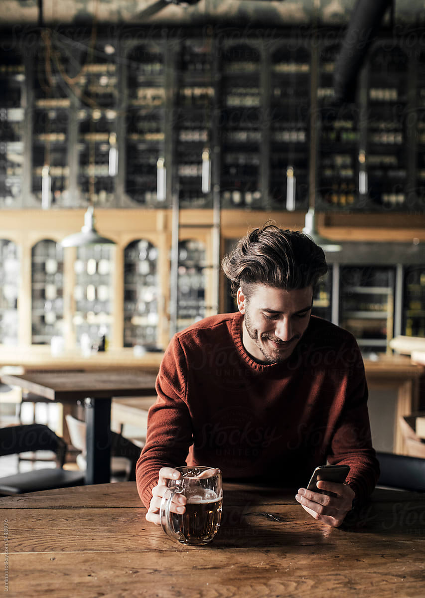 "Man Typing On Cell Phone At Bar" by Stocksy Contributor "Lumina" - Stocksy
