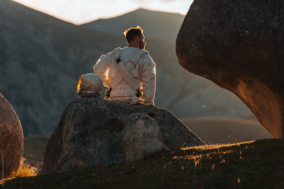 "A Weary Astronaut Rests On A Rock Looking Out On The Distance Of A ...