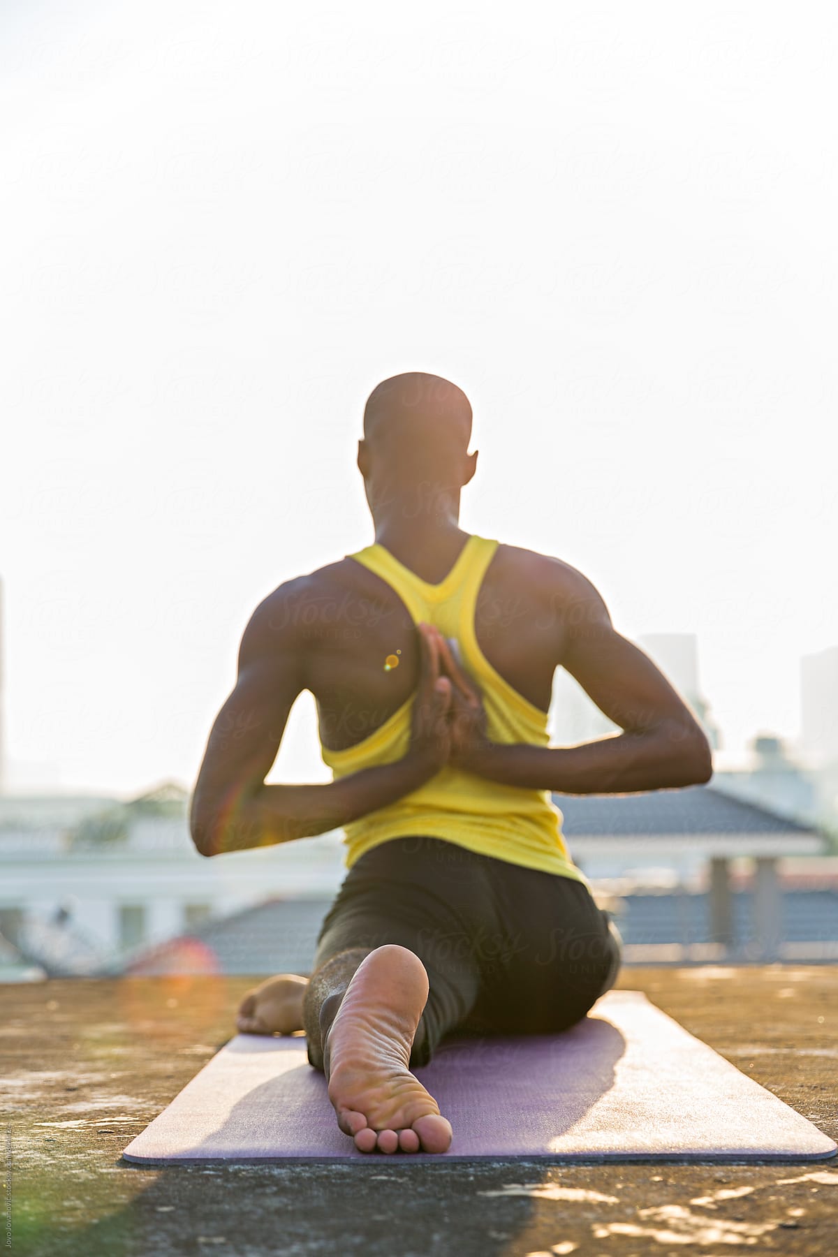 Back of a fit dark skinned man doing yoga on a city building rooftop ...
