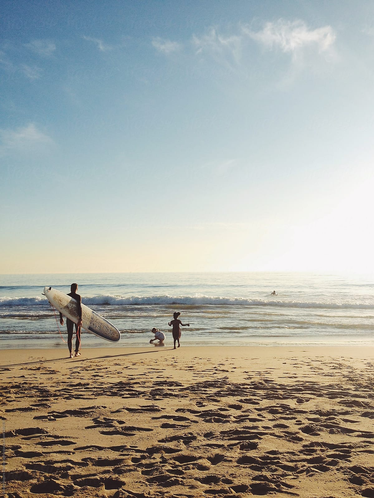 "Father Going Into Ocean To Surf With Children Playing On Sand" by ...