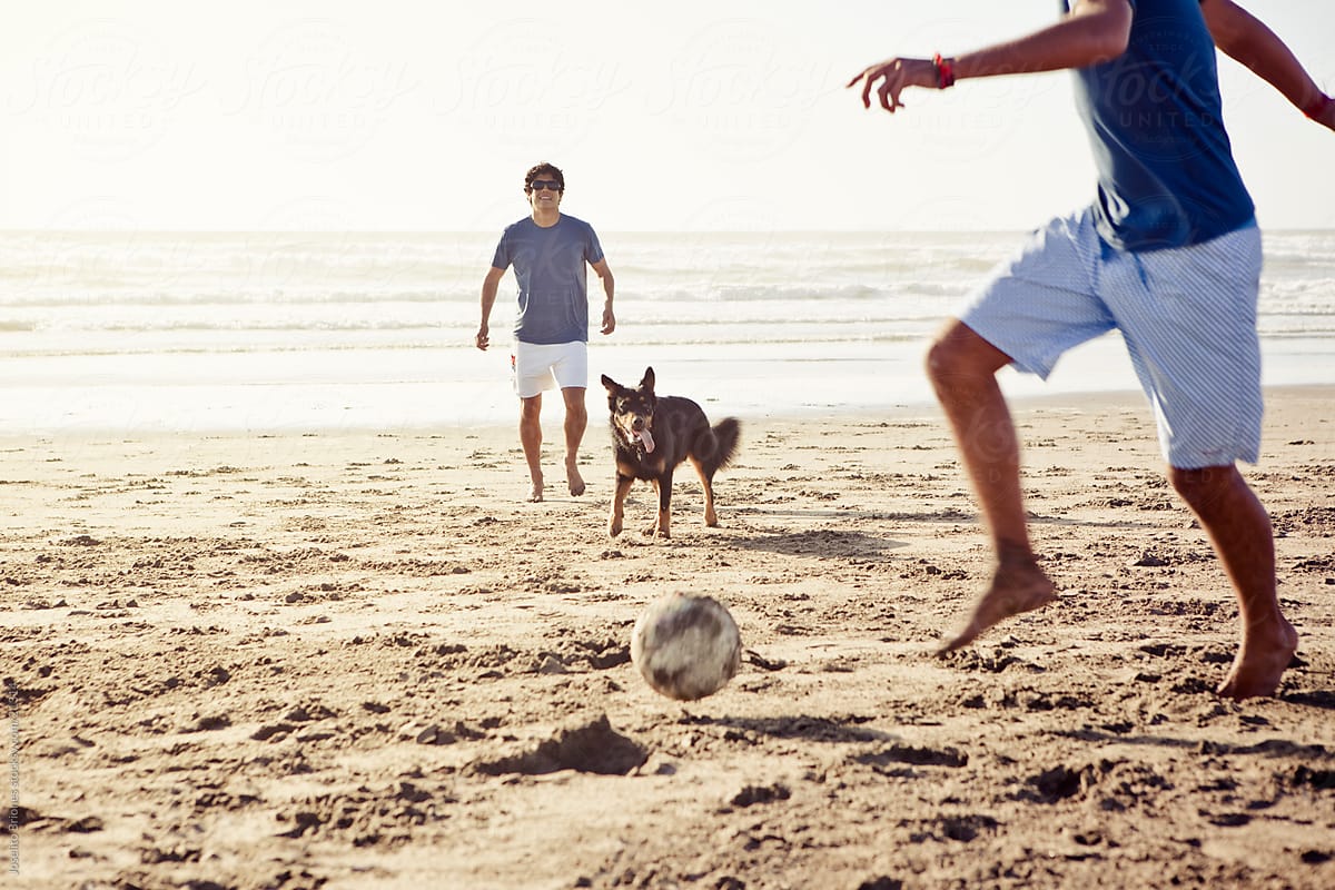 "Latino Men Playing Beach Football With Pet Dog" by Stocksy Contributor ...