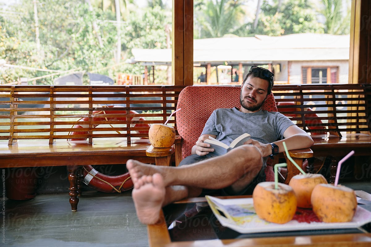 "Young Man Reading A Book With His Legs Up On A Table With Coconuts" by ...