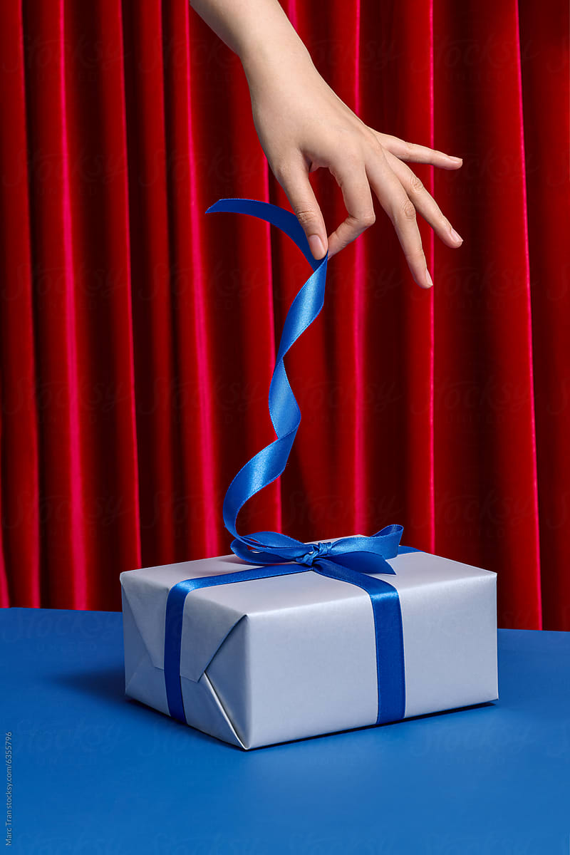 "Hand Unwrapping Blue Ribbon Gift With Red Background" by Stocksy ...