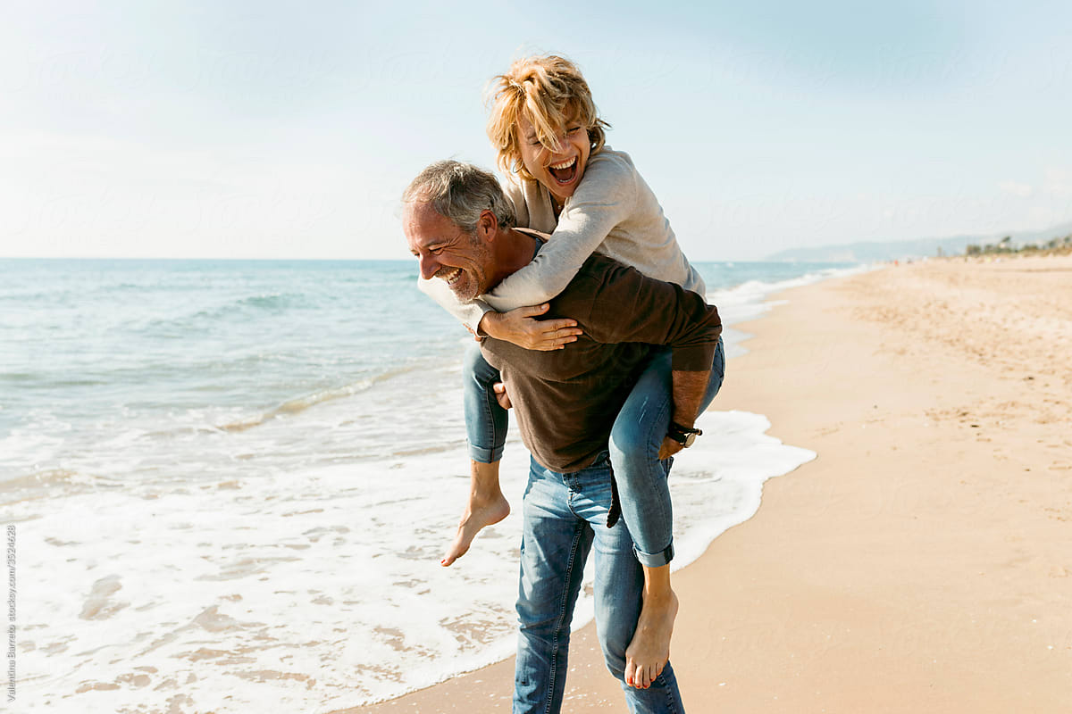 "Happy Couple Piggyback At The Beach" by Stocksy Contributor "Valbar ...