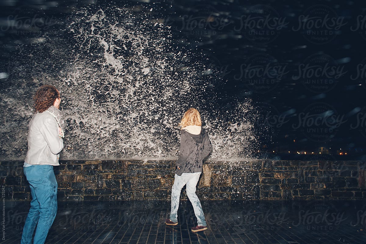 "Two Friends Running Away From The Water Splashing Up Against The ...