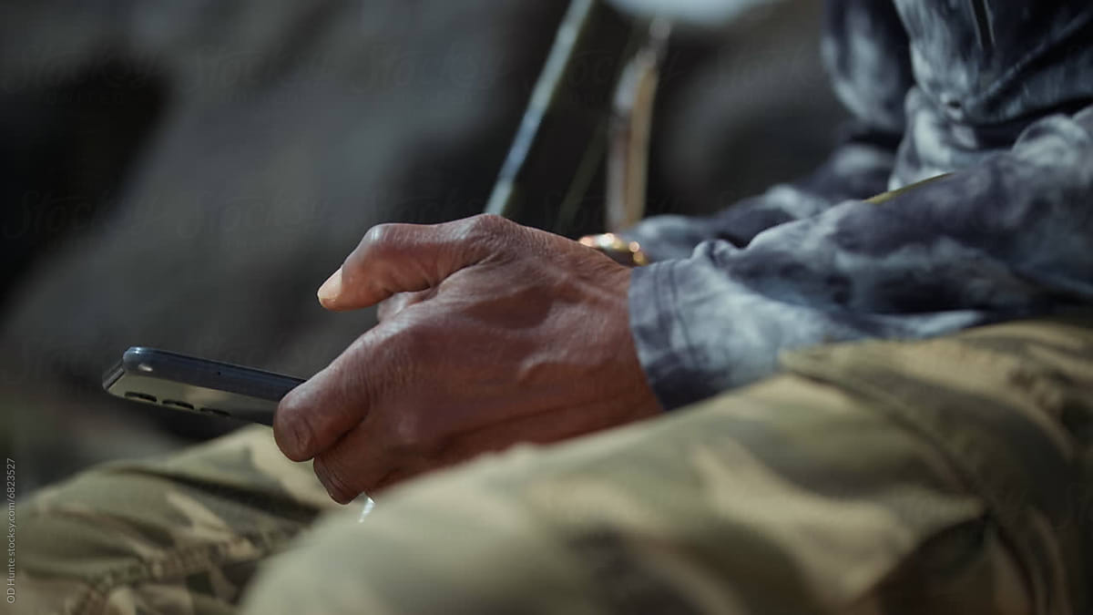 "A Mature Man Seated Outdoors Scrolling On A Non-apple Phone" by ...